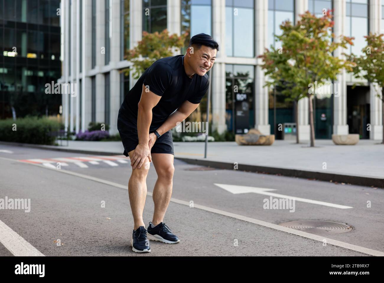 Young Asian male runner standing in the middle of the street bent over ...