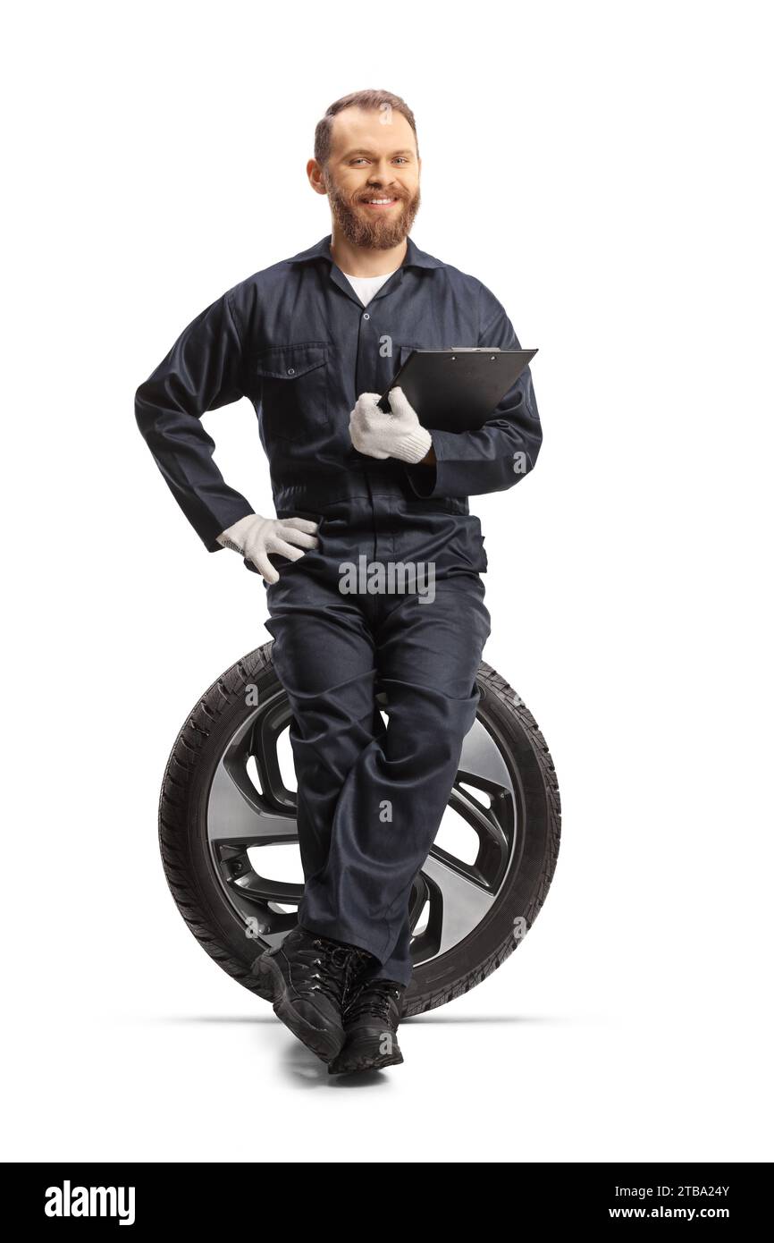 Car mechanic smiling and sitting on a tire with document in hands ...
