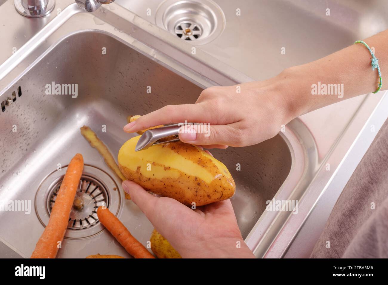 Female hands peeling a potato in sink in the kitchen. Vegetables ...