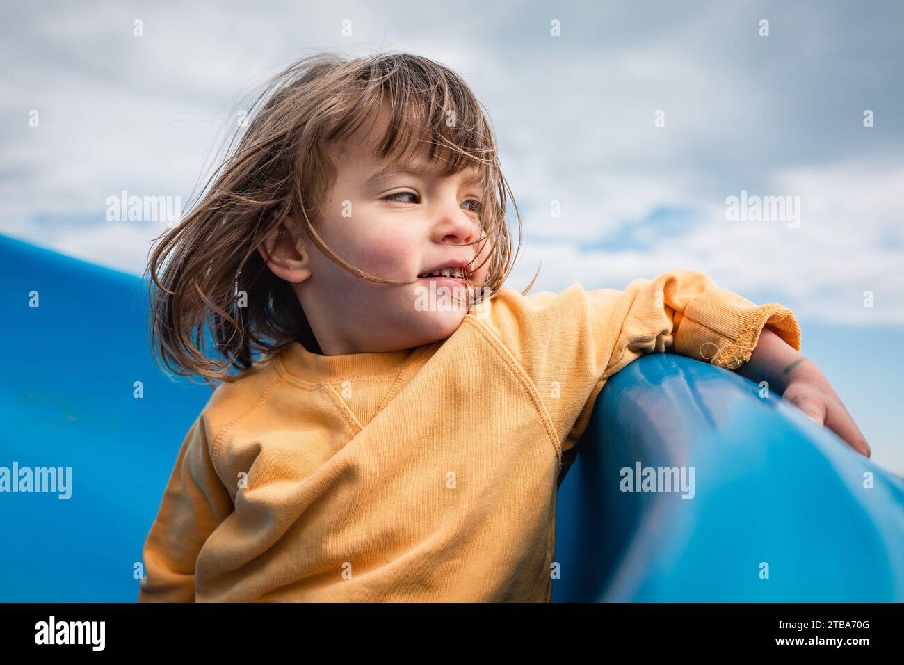 little girl in yellow clothes going down blue slide watching aside ...