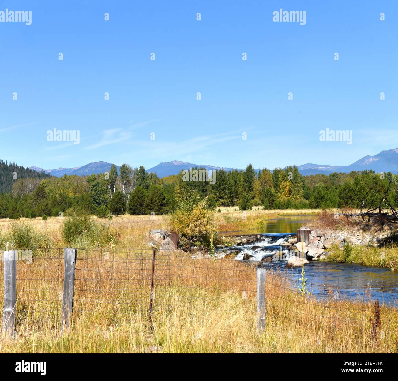 Fence runs in front of a small country stream in Oregon. Cascades rise ...