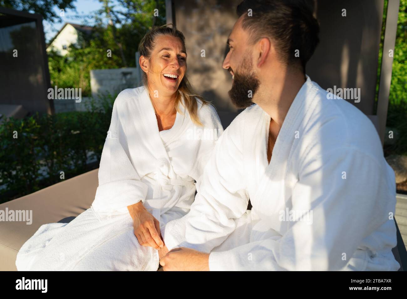 Two people in white robes sitting on a couple's lounger outdoors and ...