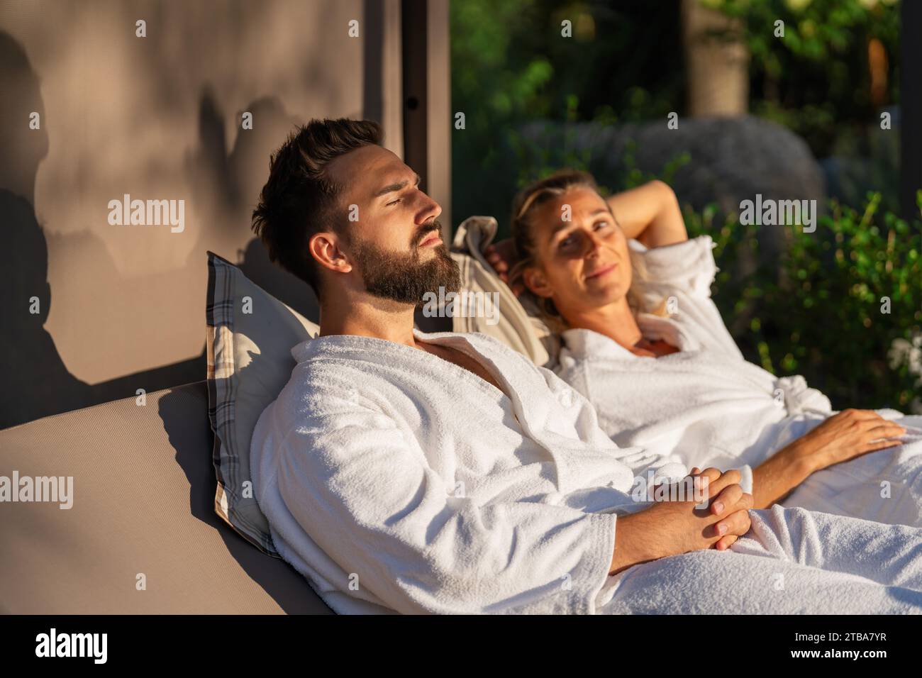 Relaxed couple in white robes lounging outdoors in the sunlight Stock ...