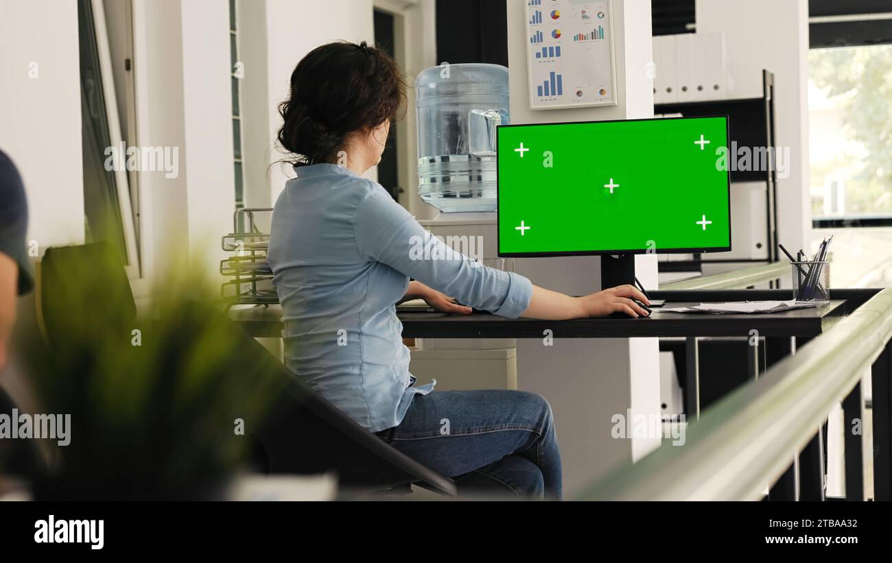 Office worker checks greenscreen monitor at desk, working on business ...