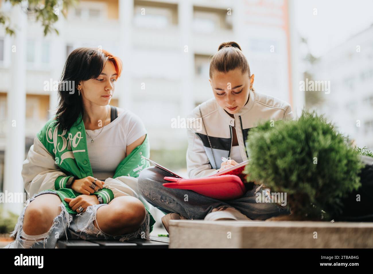Two high school girls outdoors studying together, sharing knowledge ...