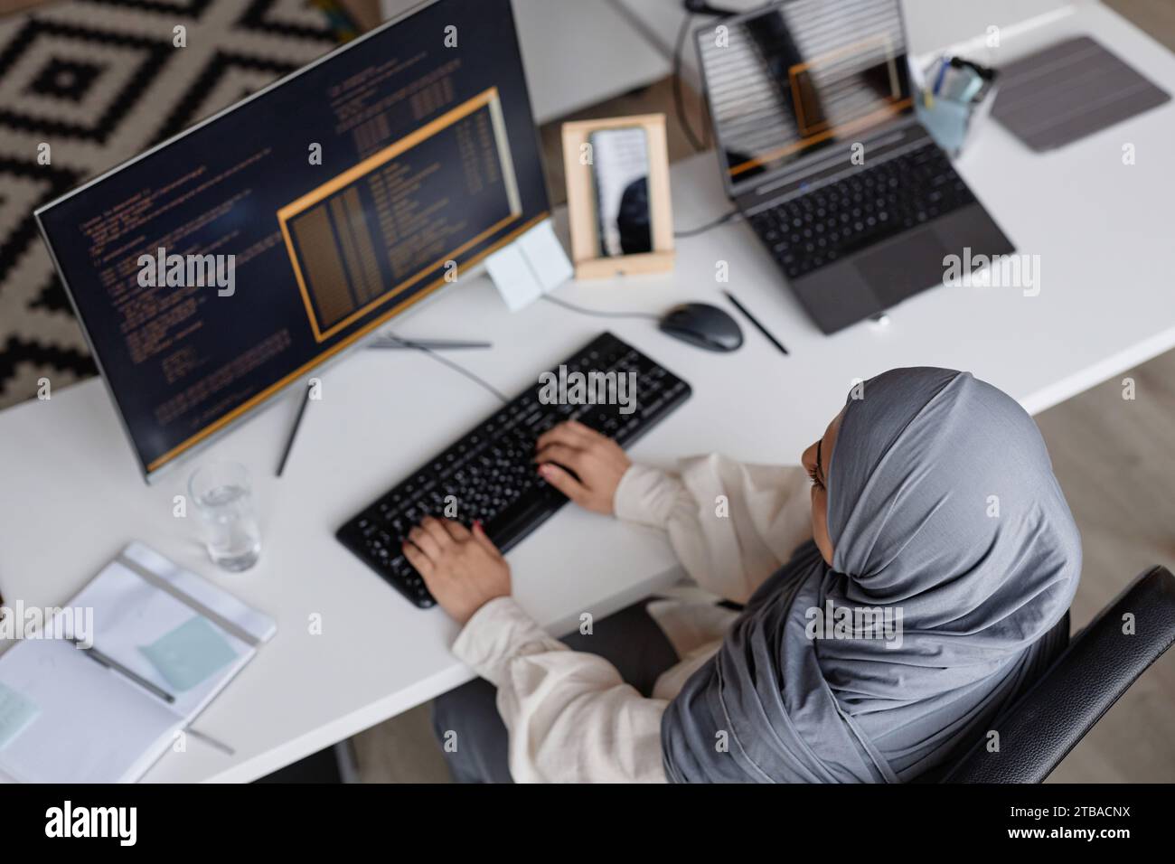 Top view at Muslim young woman writing code with multiple computer devices and wearing modest ...