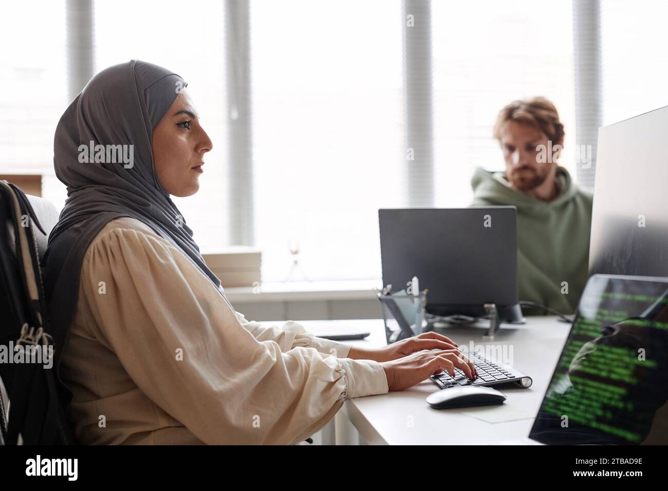Side view portrait of young Middle-Eastern woman as female programmer using computer in office ...