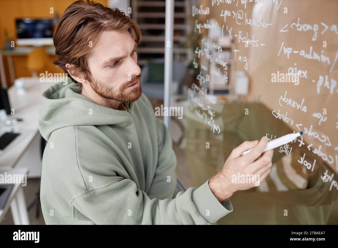 Side view at bearded young man writing data code ideas on glass in ...