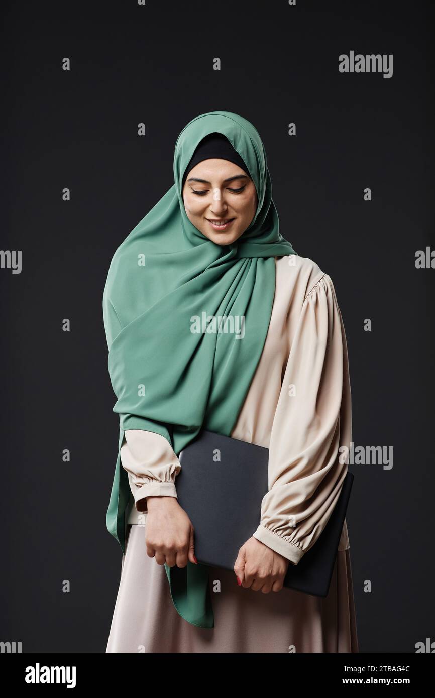 Vertical portrait of modest Muslim woman holding laptop and smiling ...