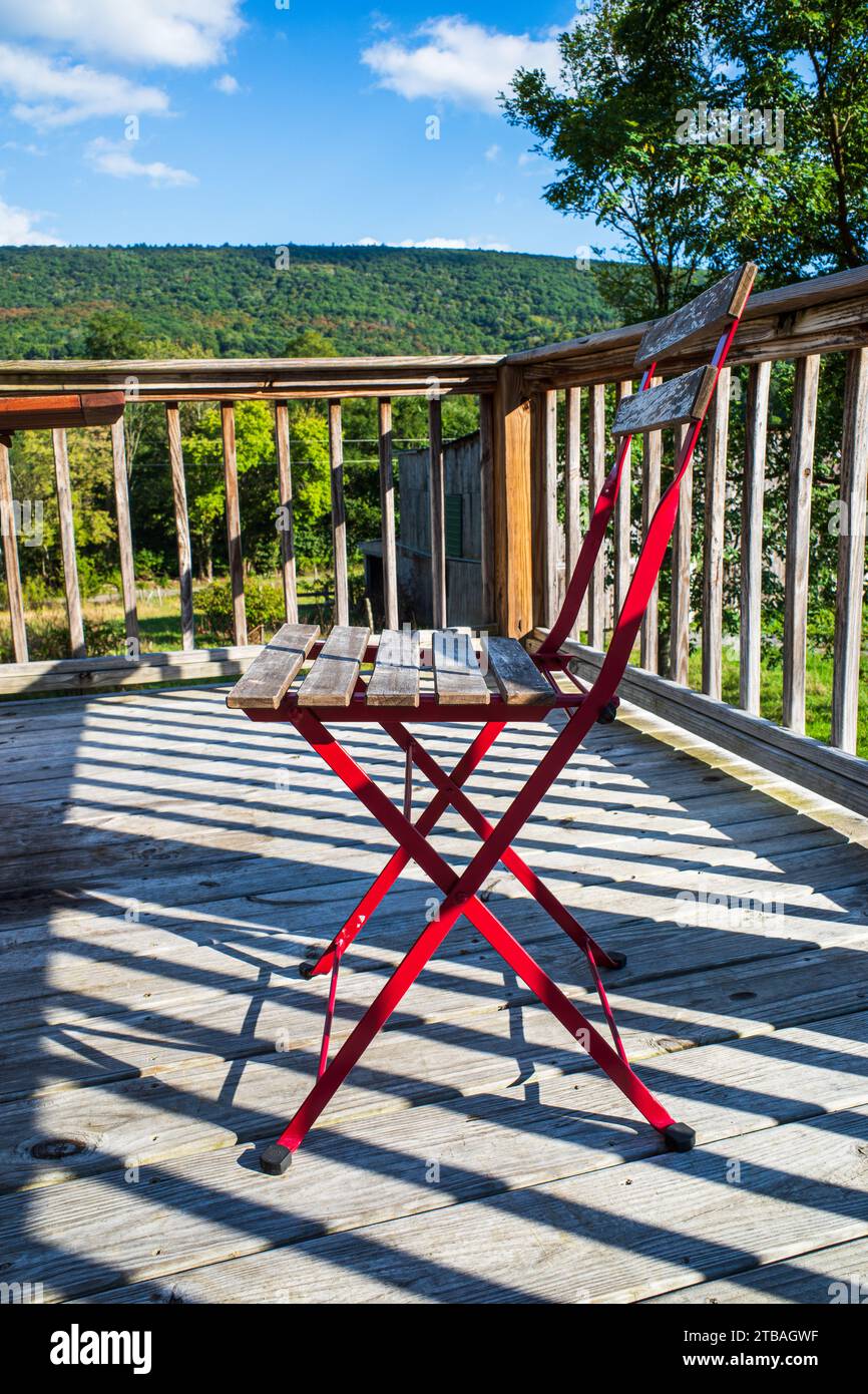 Set upon a wooden deck, a red-legged chair overlooks a backdrop of tree ...