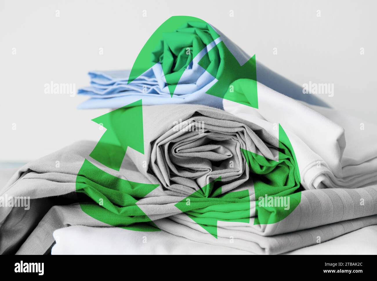 Heap of clothes and recycling symbol on light background. Ecology ...