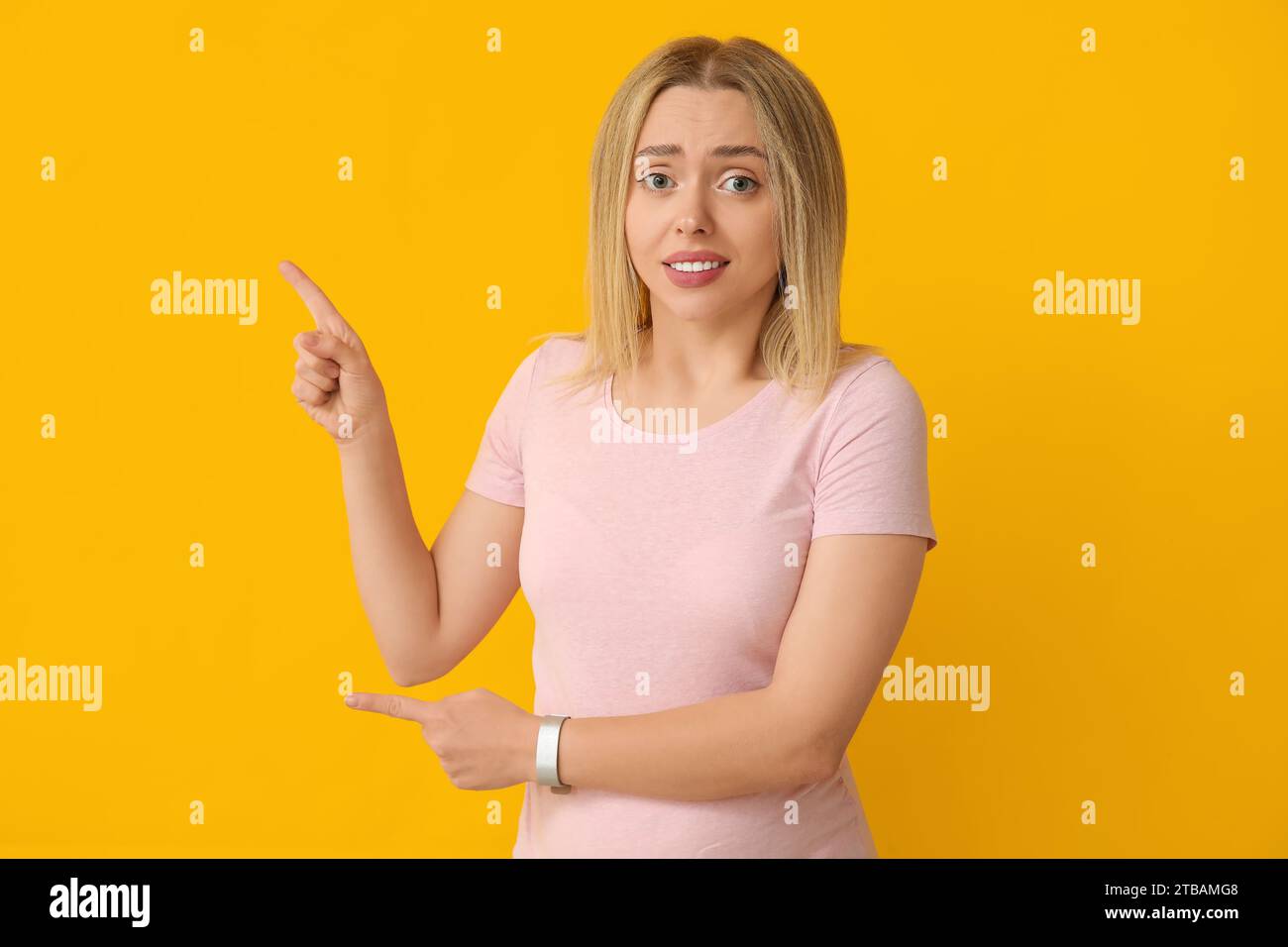Embarrassed young woman pointing at something on yellow background ...