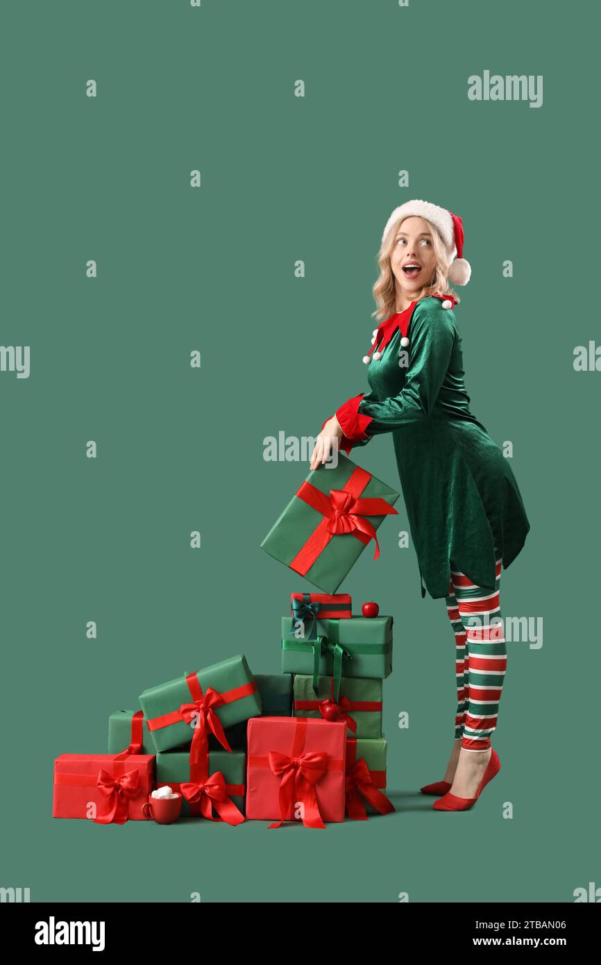 Beautiful young woman dressed as elf with Christmas gifts on green ...
