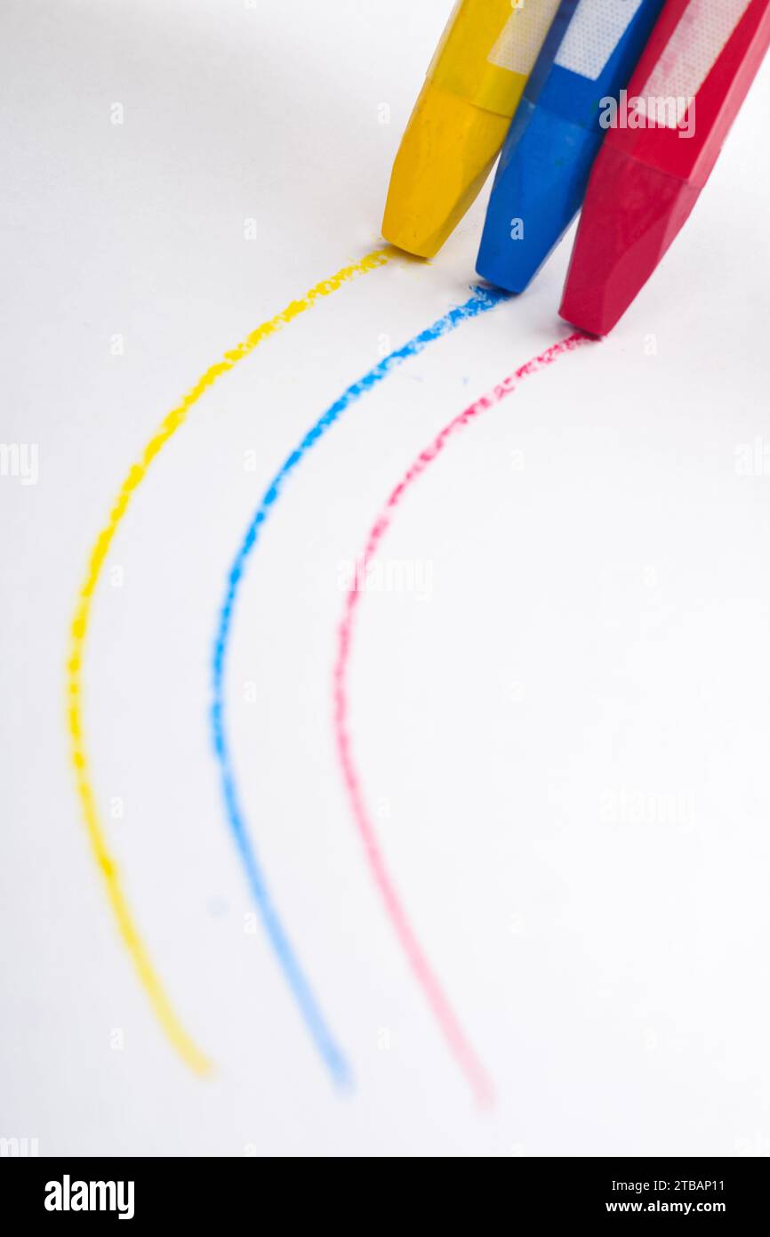 three colored crayon sticks draw lines forming a curve on white paper ...