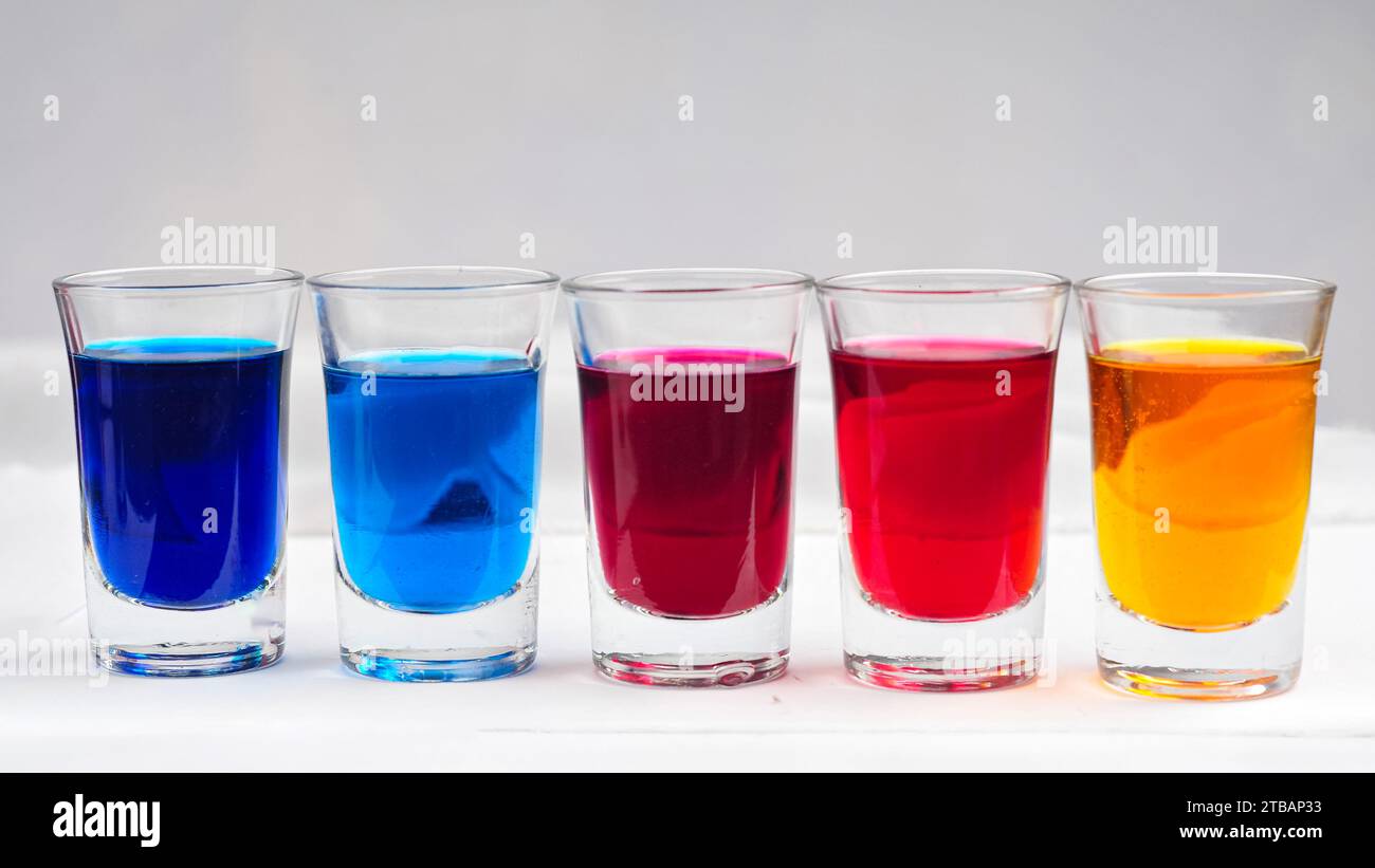 Small glasses filled with colorful water are neatly arranged on an ...