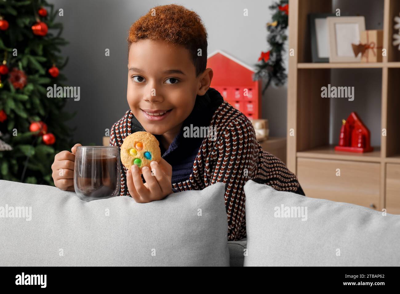 Cute little African-American boy eating cookie with hot chocolate at ...