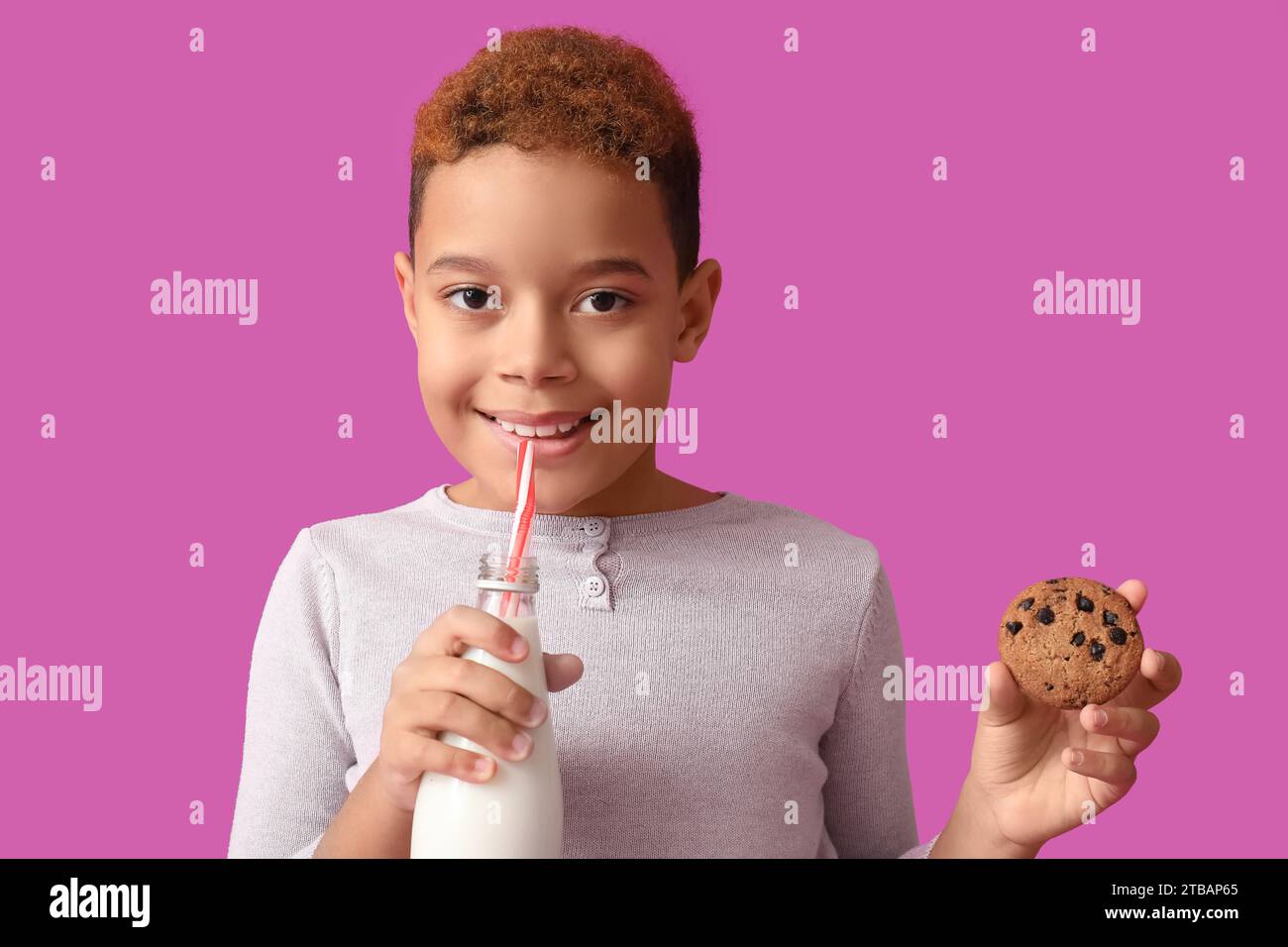 Cute little African-American boy eating cookie with milk on purple ...