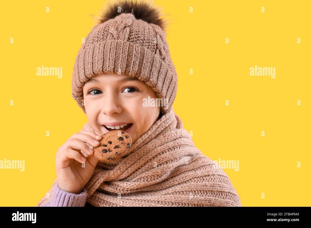 Cute little girl eating cookie on yellow background Stock Photo - Alamy