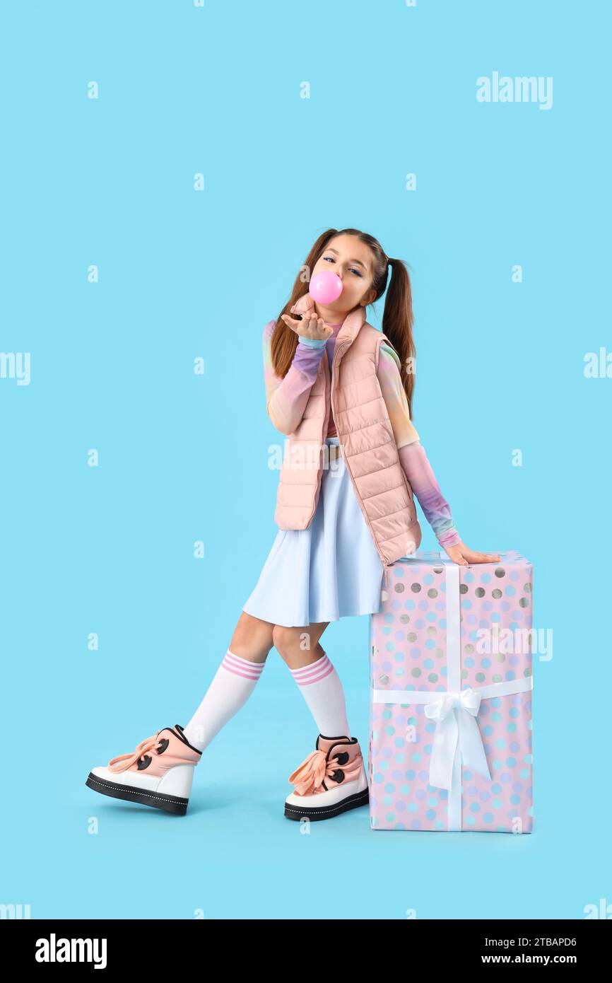 Trendy girl with gift box blowing bubble gum on blue background Stock ...