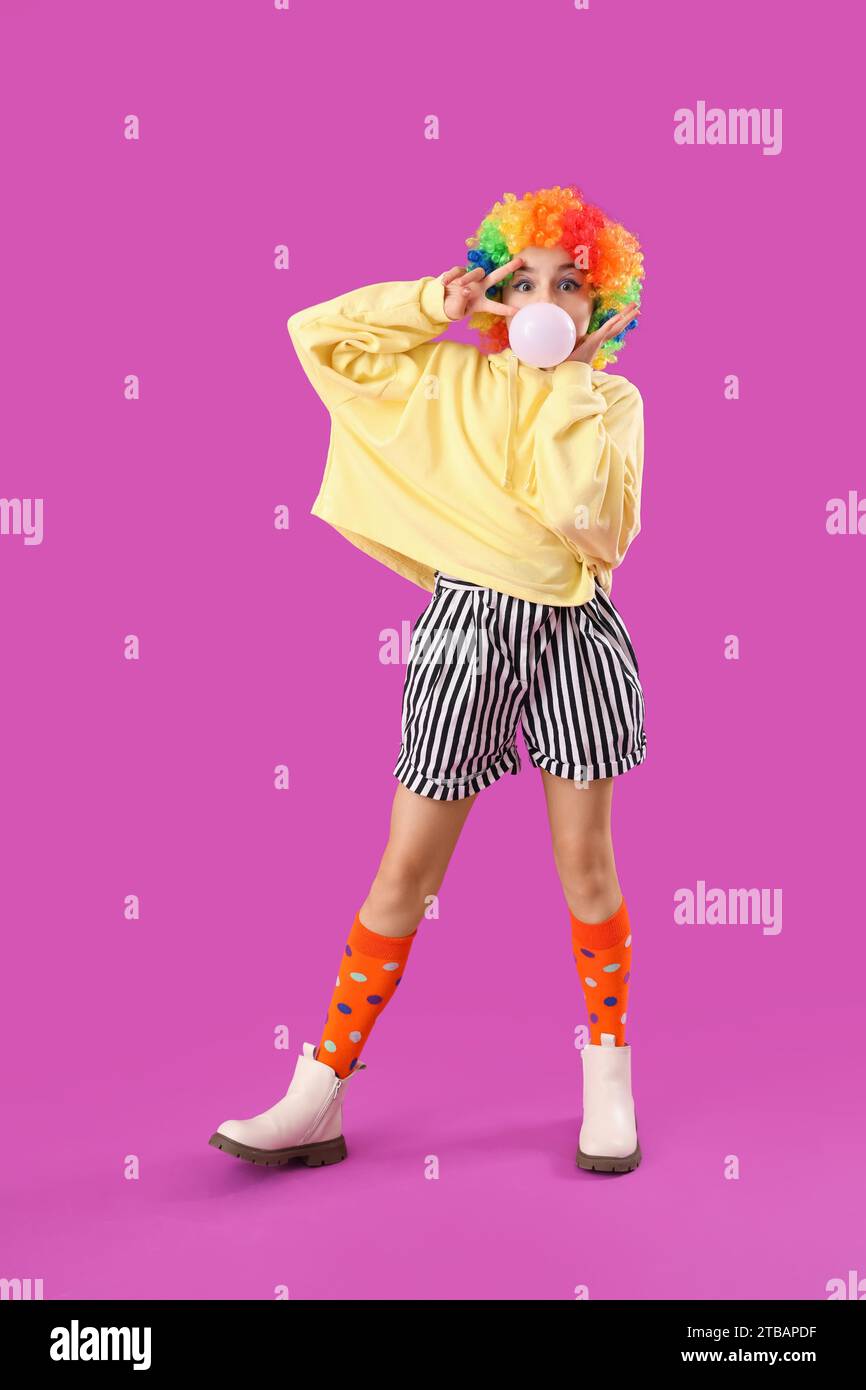 Trendy girl in clown costume blowing bubble gum on purple background ...