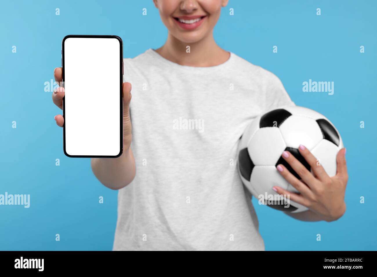 Happy sports fan with soccer ball and smartphone on light blue ...