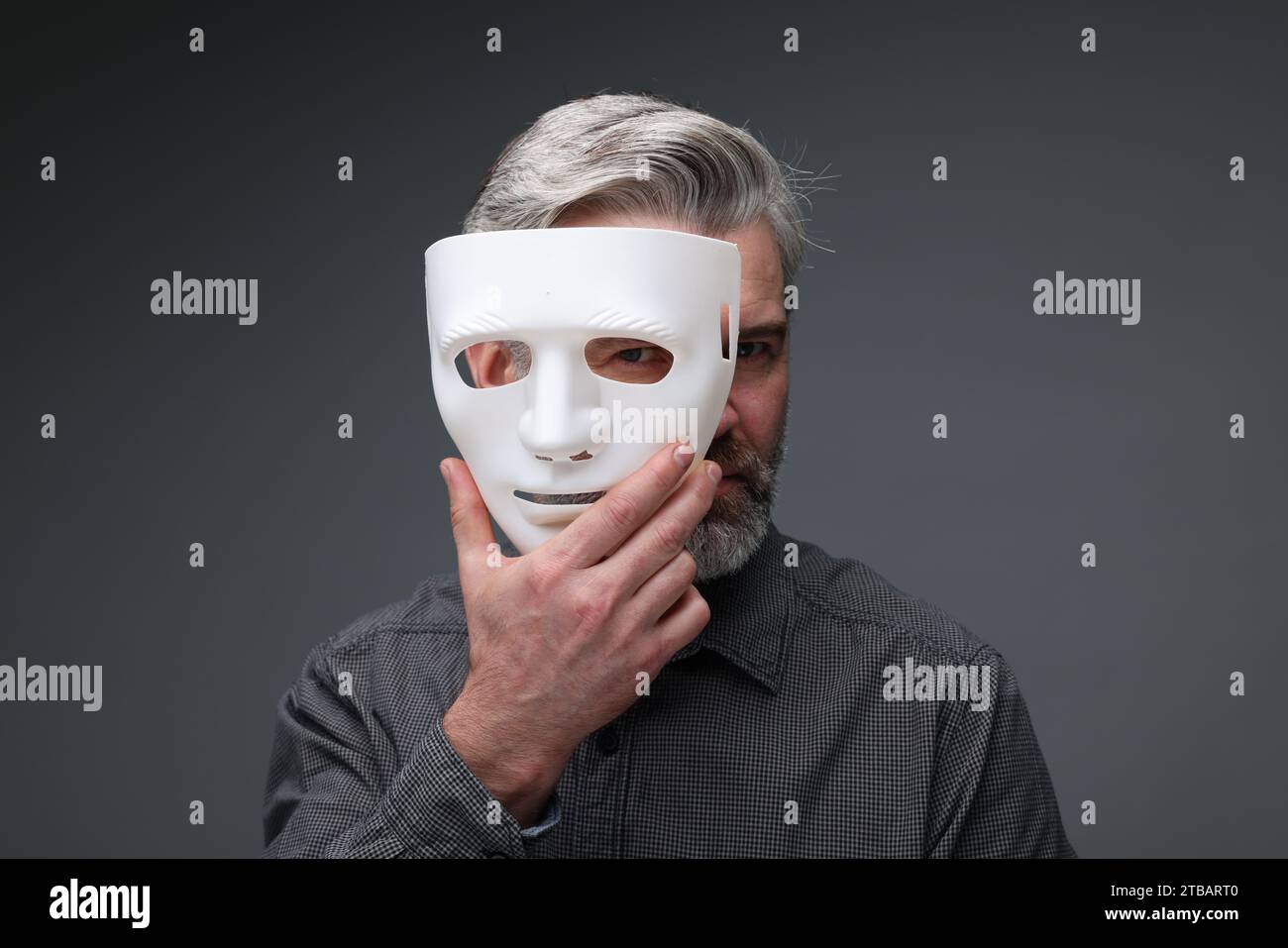 Multiple personality concept. Man covering face with mask on dark grey ...