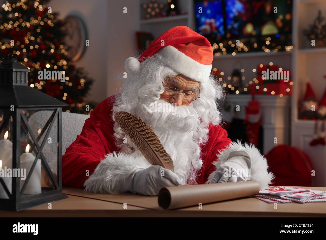 Santa Claus writing letter at table in room decorated for Christmas ...