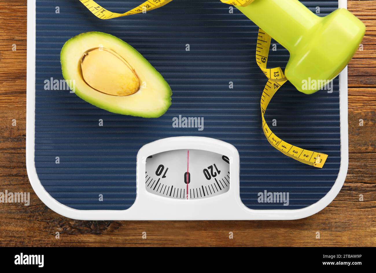 Healthy diet. Scale, avocado, measuring tape and dumbbell on wooden ...
