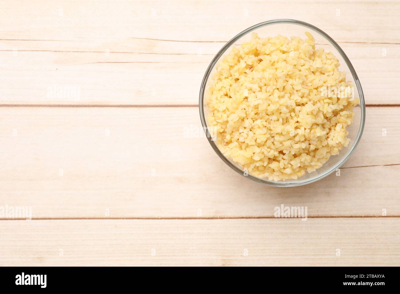 Delicious bulgur in glass bowl on wooden table, top view. Space for ...