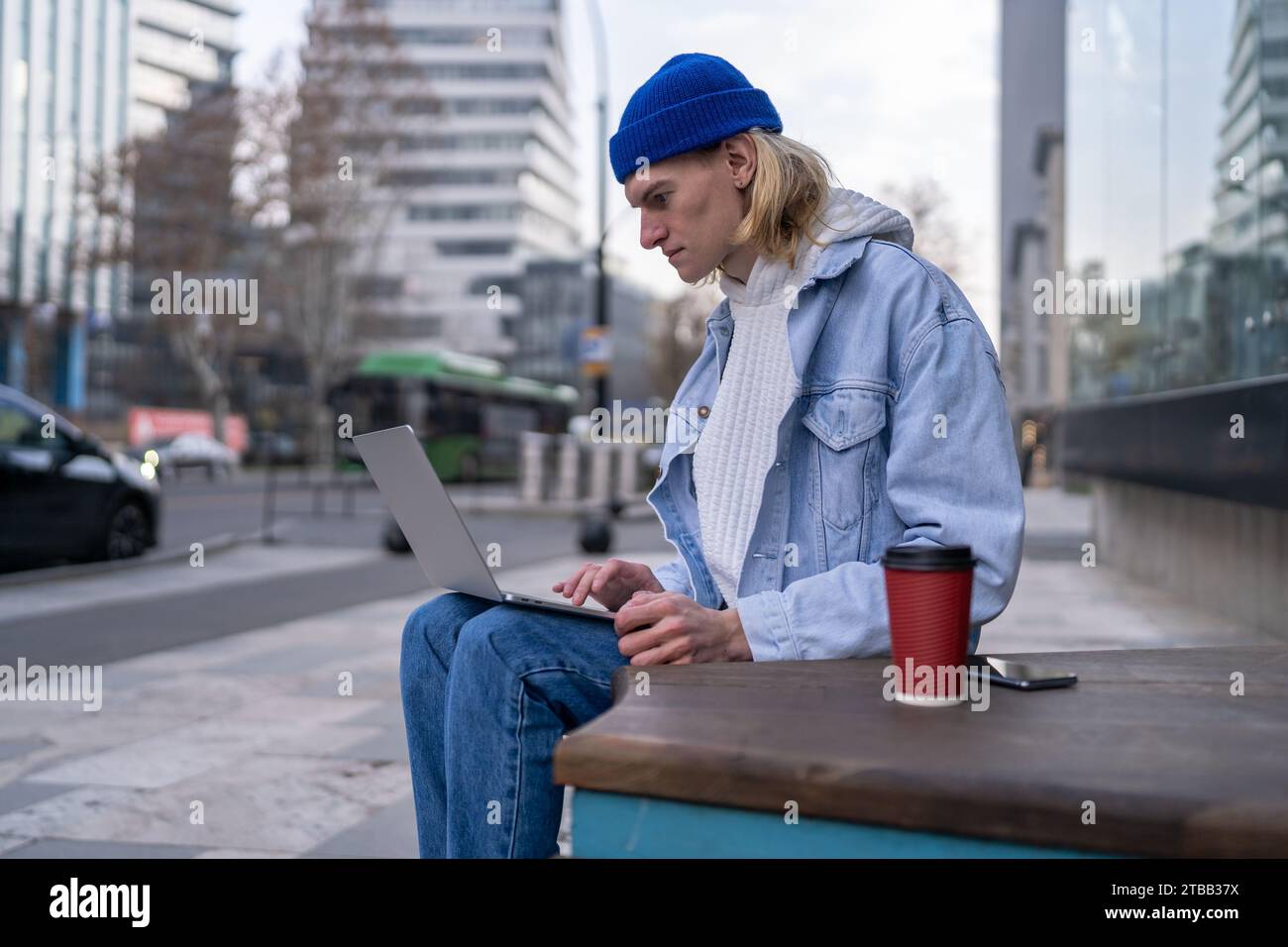 Fashionable guy sitting in urban street searching info in laptop ...