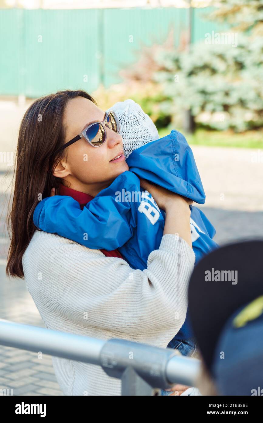 Caring mother comforts little child crying on shoulder on city street ...