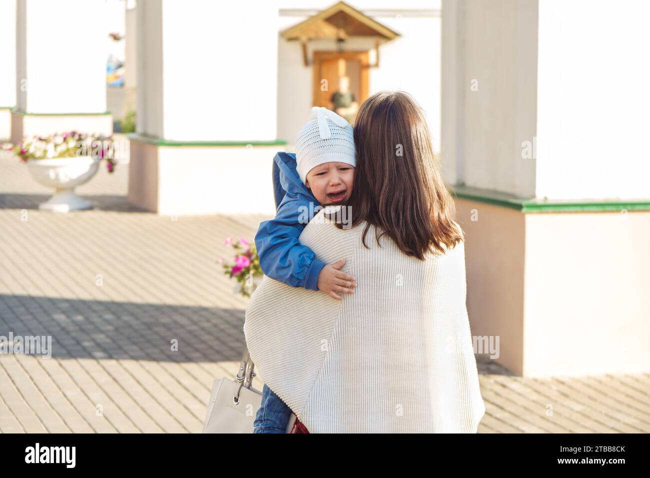Caring mother comforts little child crying on shoulder on city street ...