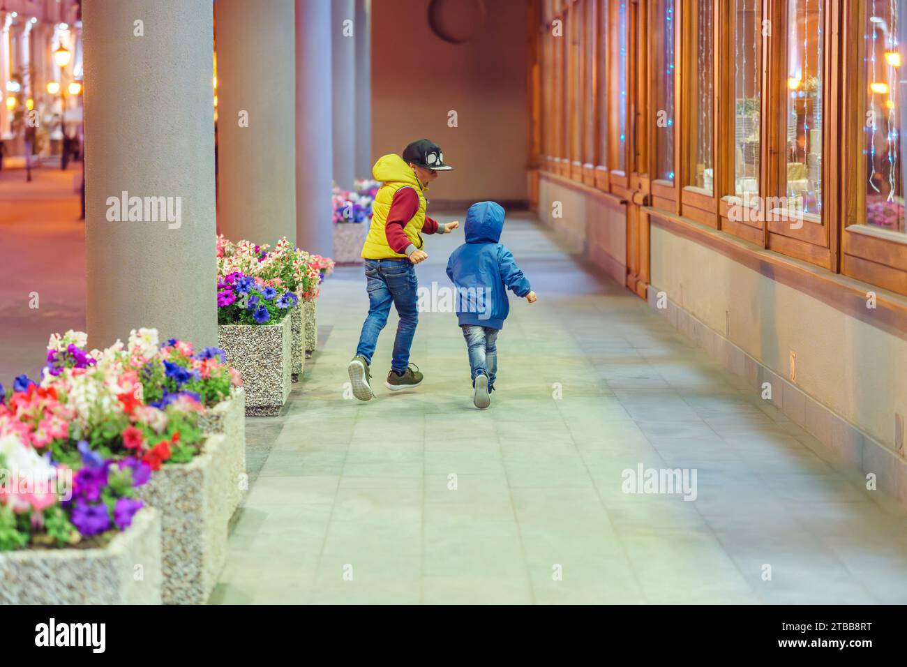 Happy little boys runs together along gallery between columns row with ...