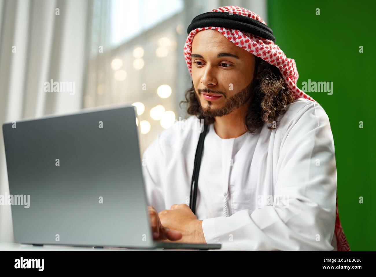 Young Arab man in traditional dress thobe working on computer in office ...