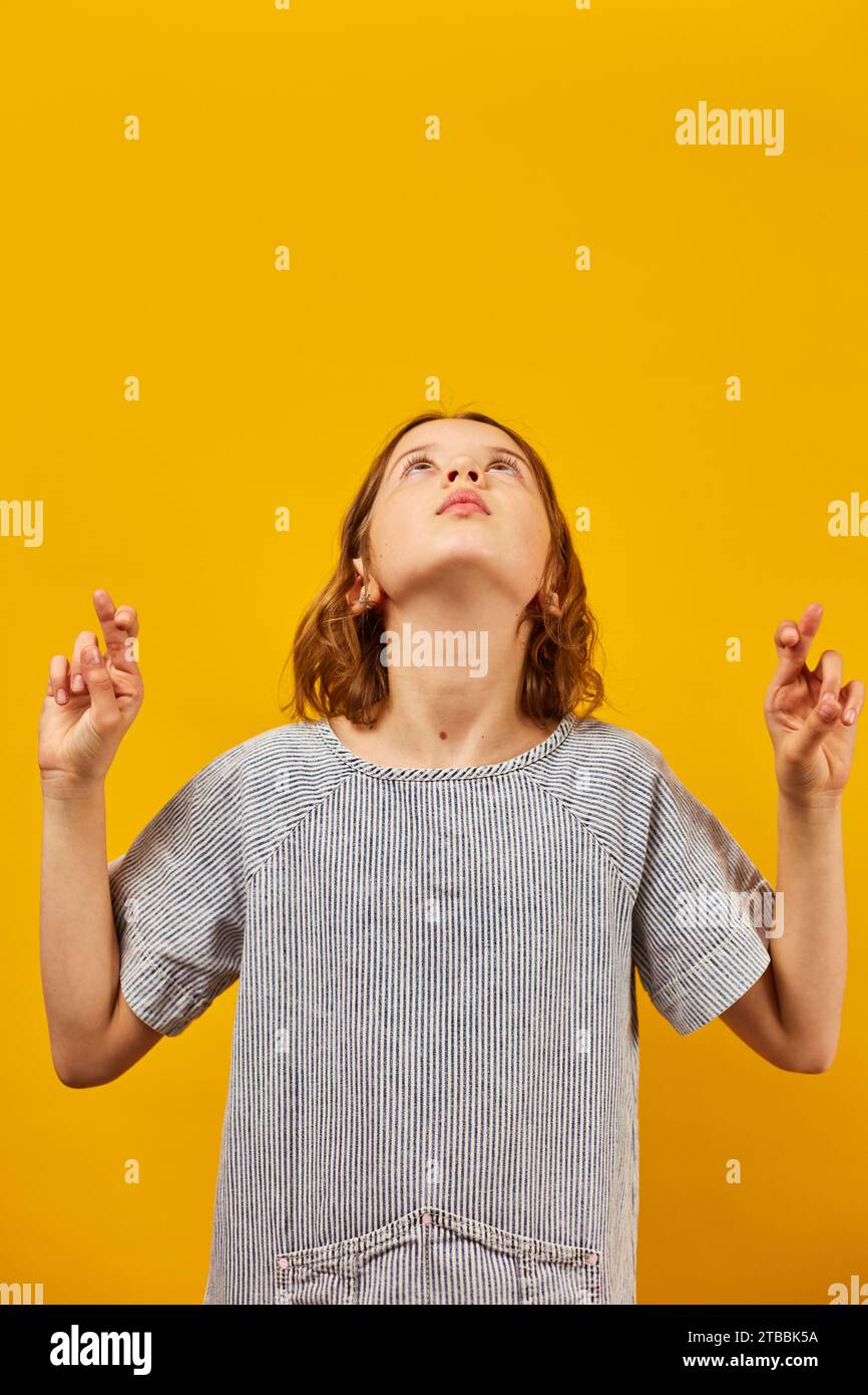 Teen girl fingers crossed on yellow studio background Stock Photo - Alamy