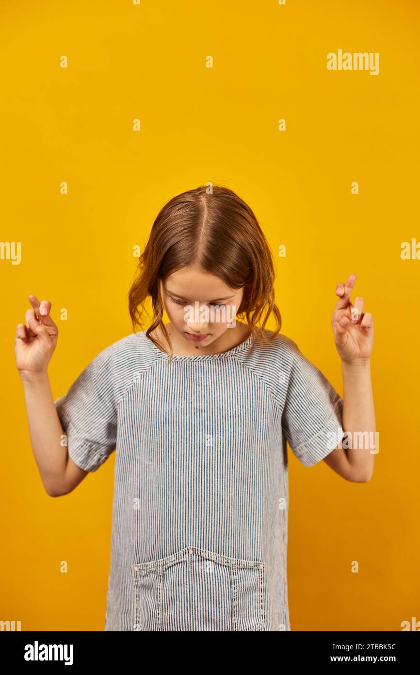 Teen girl fingers crossed on yellow studio background Stock Photo - Alamy