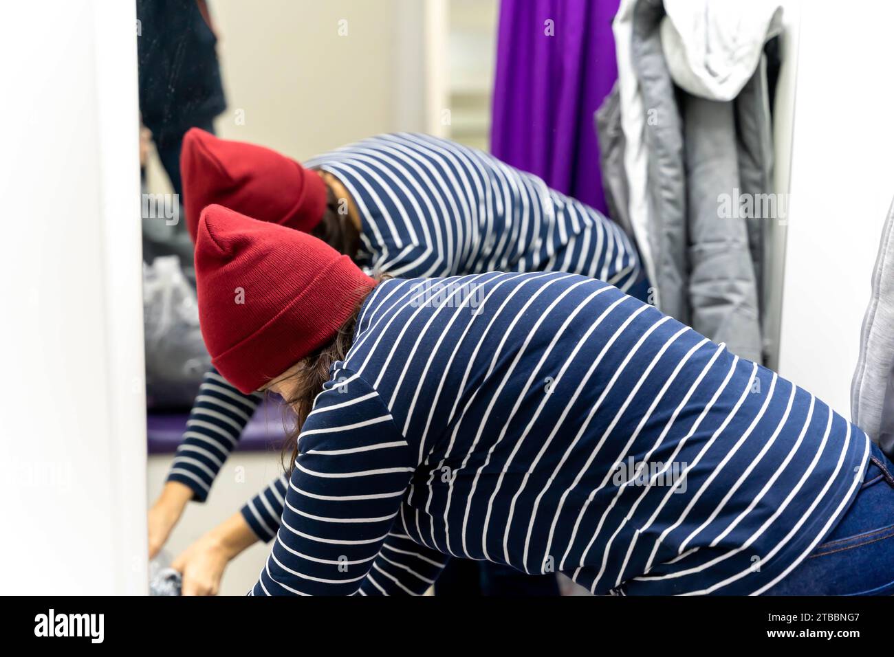 a middle-aged woman tries on a jacket and hat in the fitting room of ...
