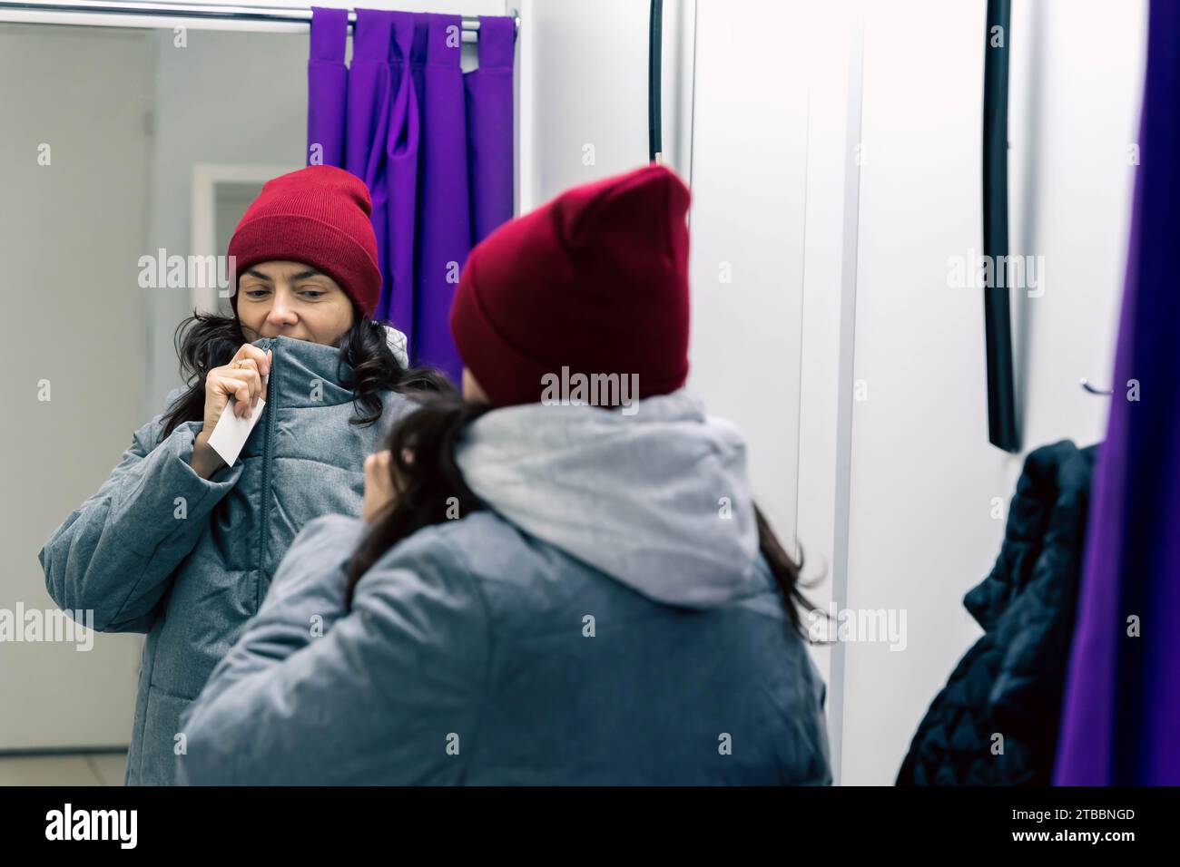 a middle-aged woman tries on a jacket and hat in the fitting room of ...