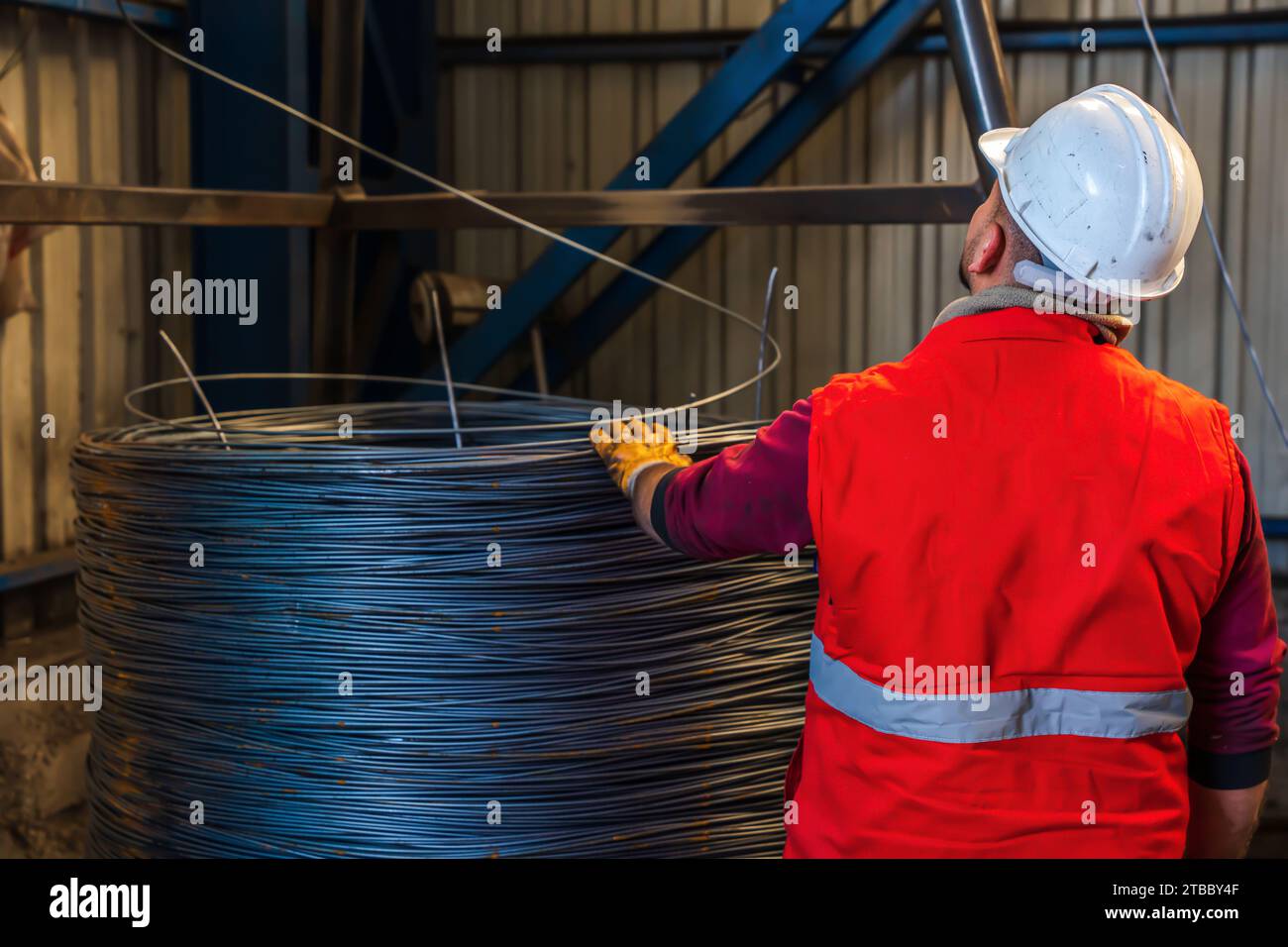 Worker or man holding Coils of iron or steel wire stacked in the metal ...