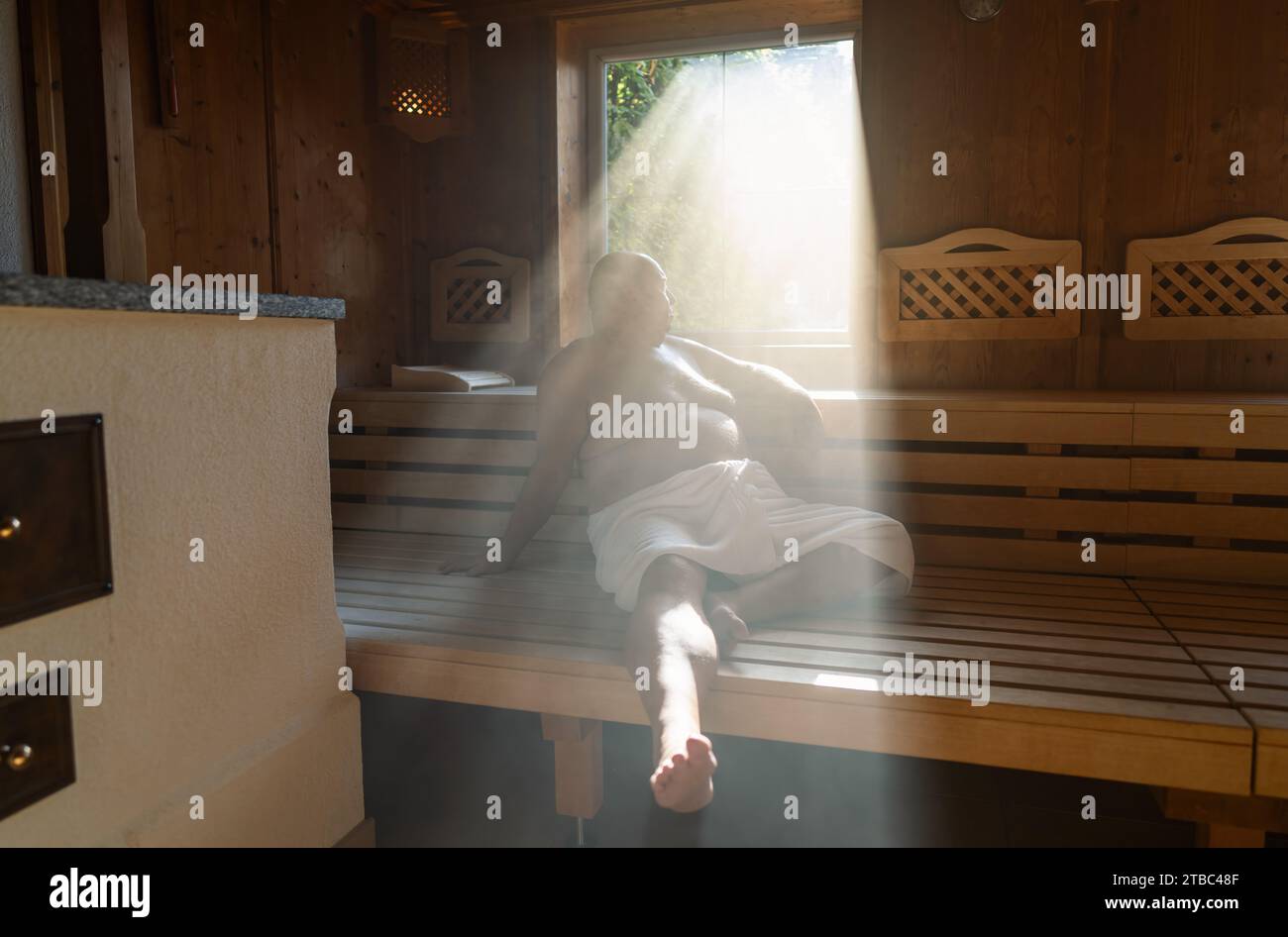 Man sitting in a sauna with light streaming through the window onto his ...