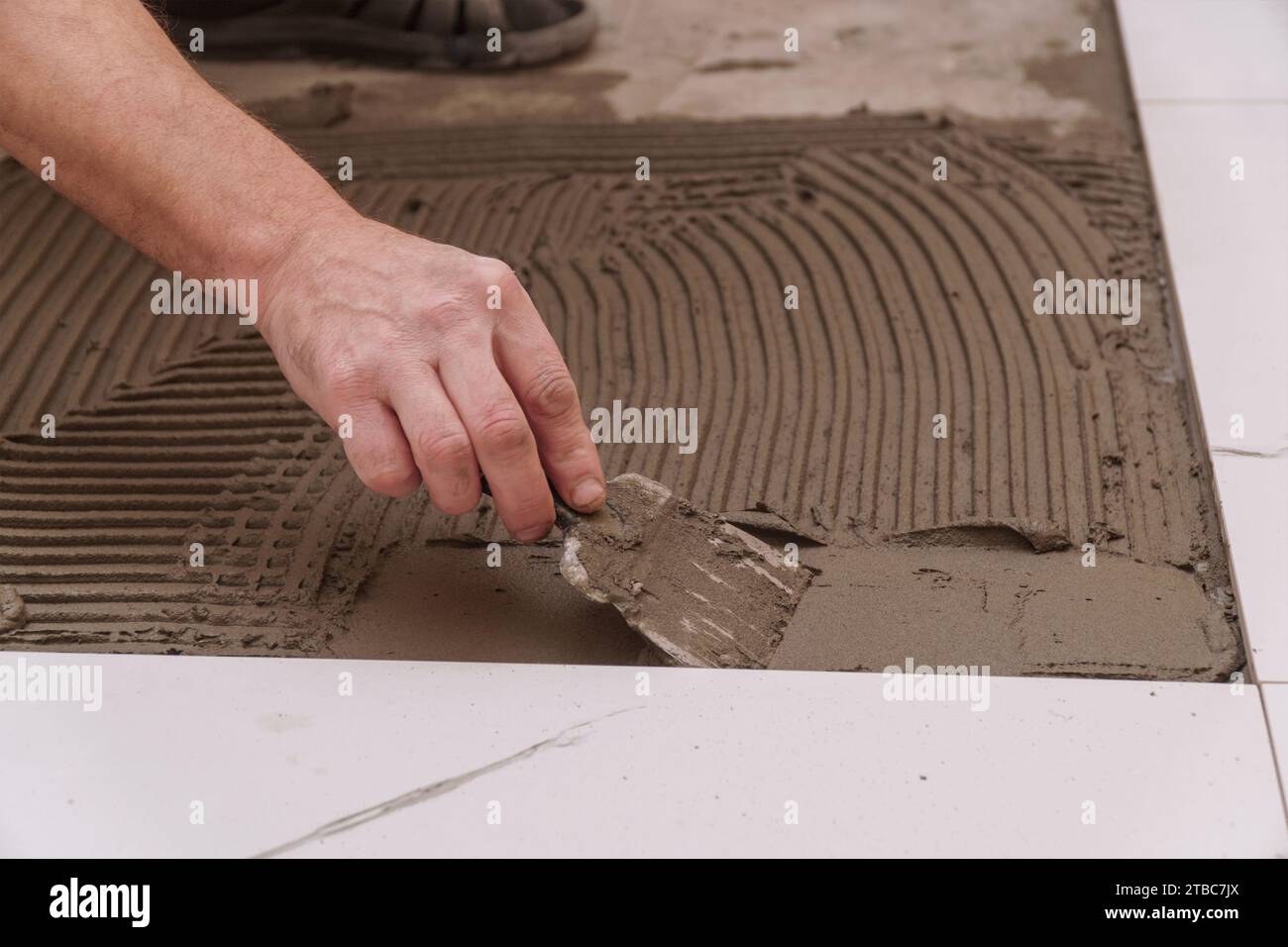 A construction worker applies cement for laying floor ceramic tiles ...
