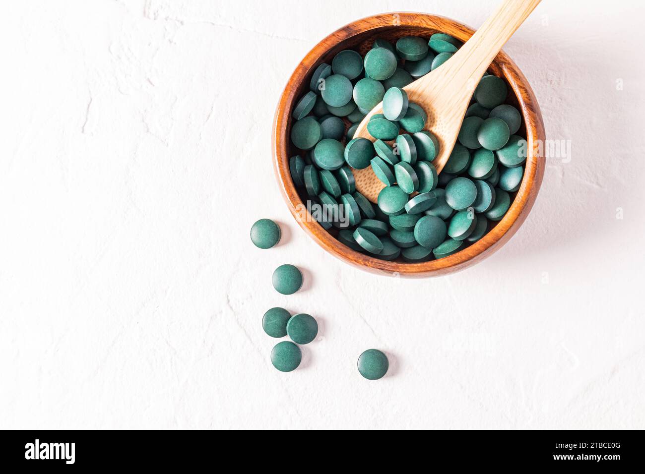 Round green spirulina algae pills in wooden bowl and spoon on white ...