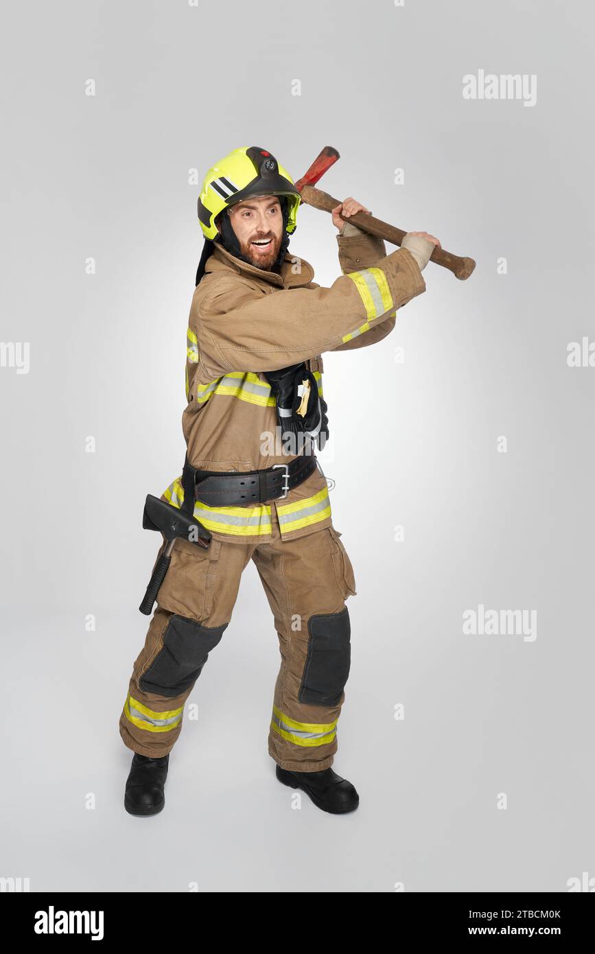 Brave caucasian firefighter battling fire, while using axe. Front view ...