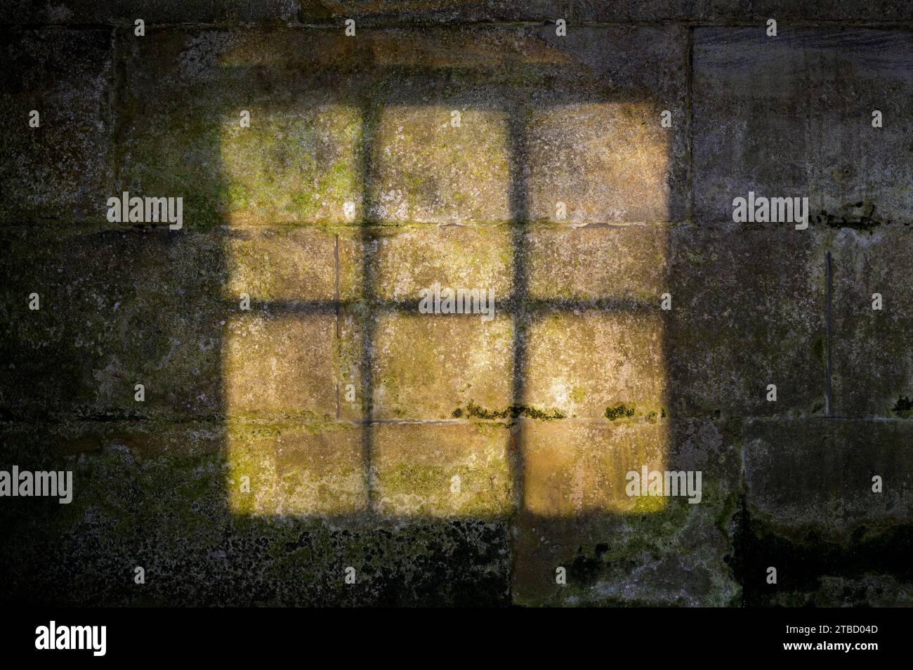 Soft light shining through a window frame on to an old stone wall with ...