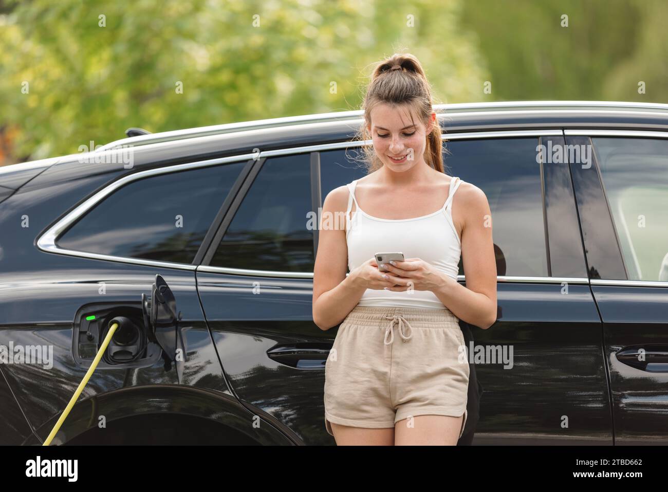 Beautiful girl plugging a cable charger into her parked black electric ...