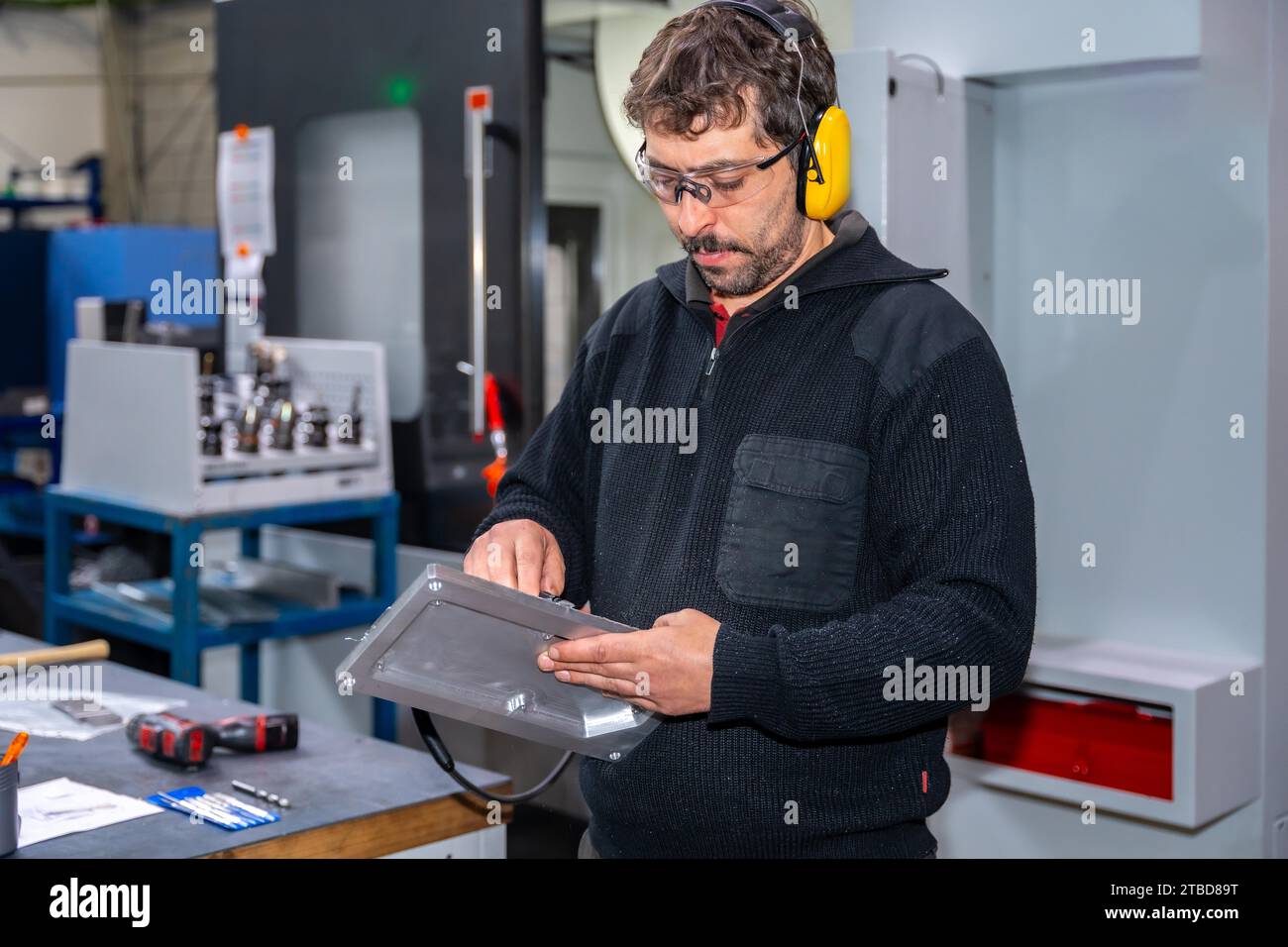 Male engineer standing on a cnc factory using safety headphones working ...