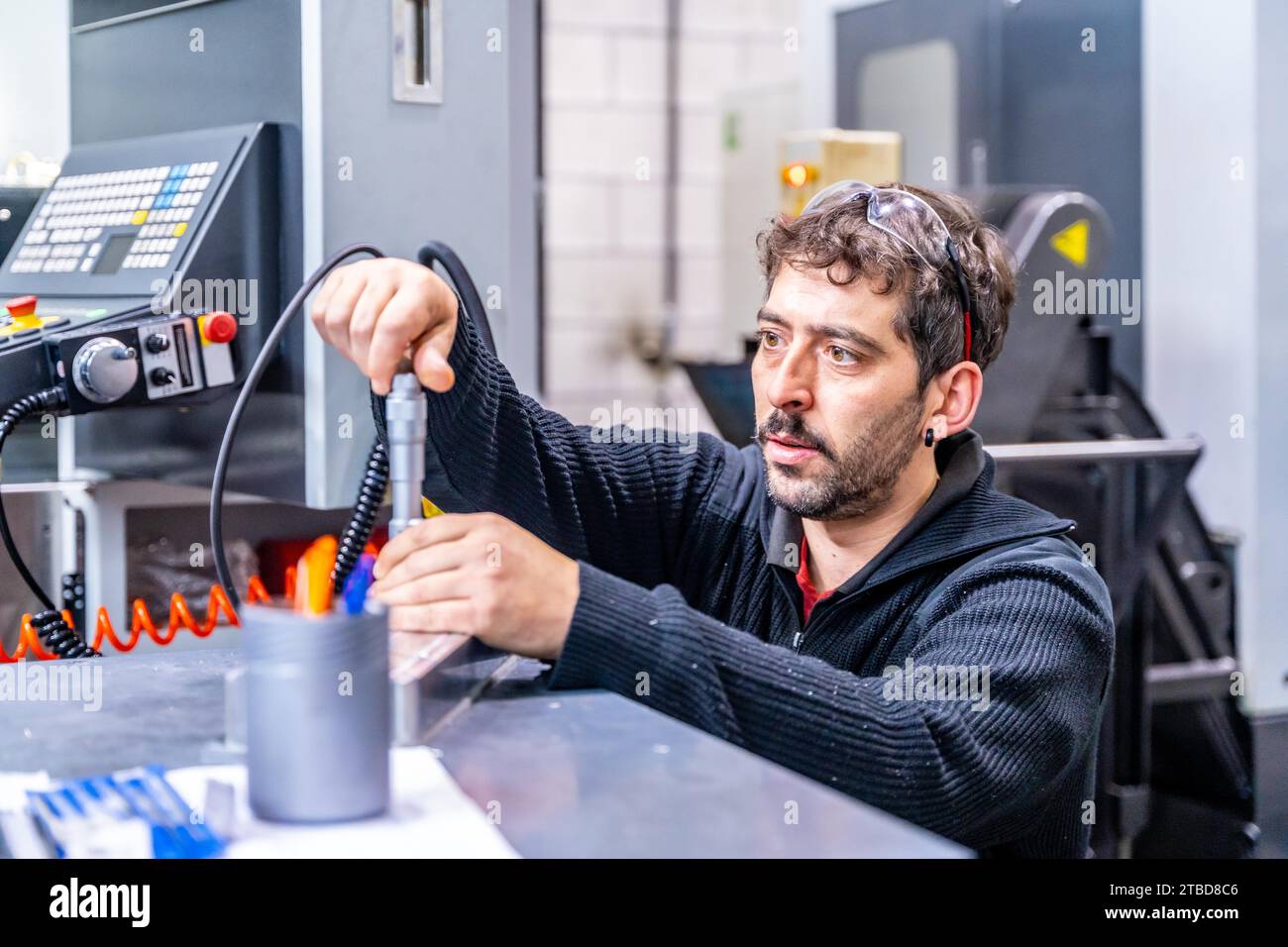 Concentrated engineer crouching fixing a piece of metal in a cnc modern ...