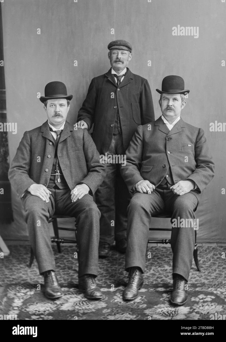 Edwardian formal studio portrait of three men in suits, two sitting and ...
