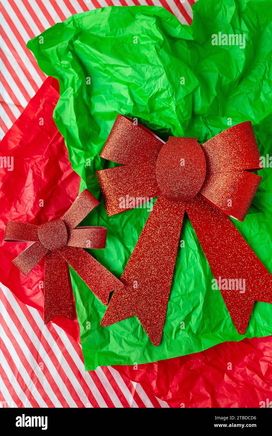 A photo of two red glittery bows on a green and red crumpled tissue ...