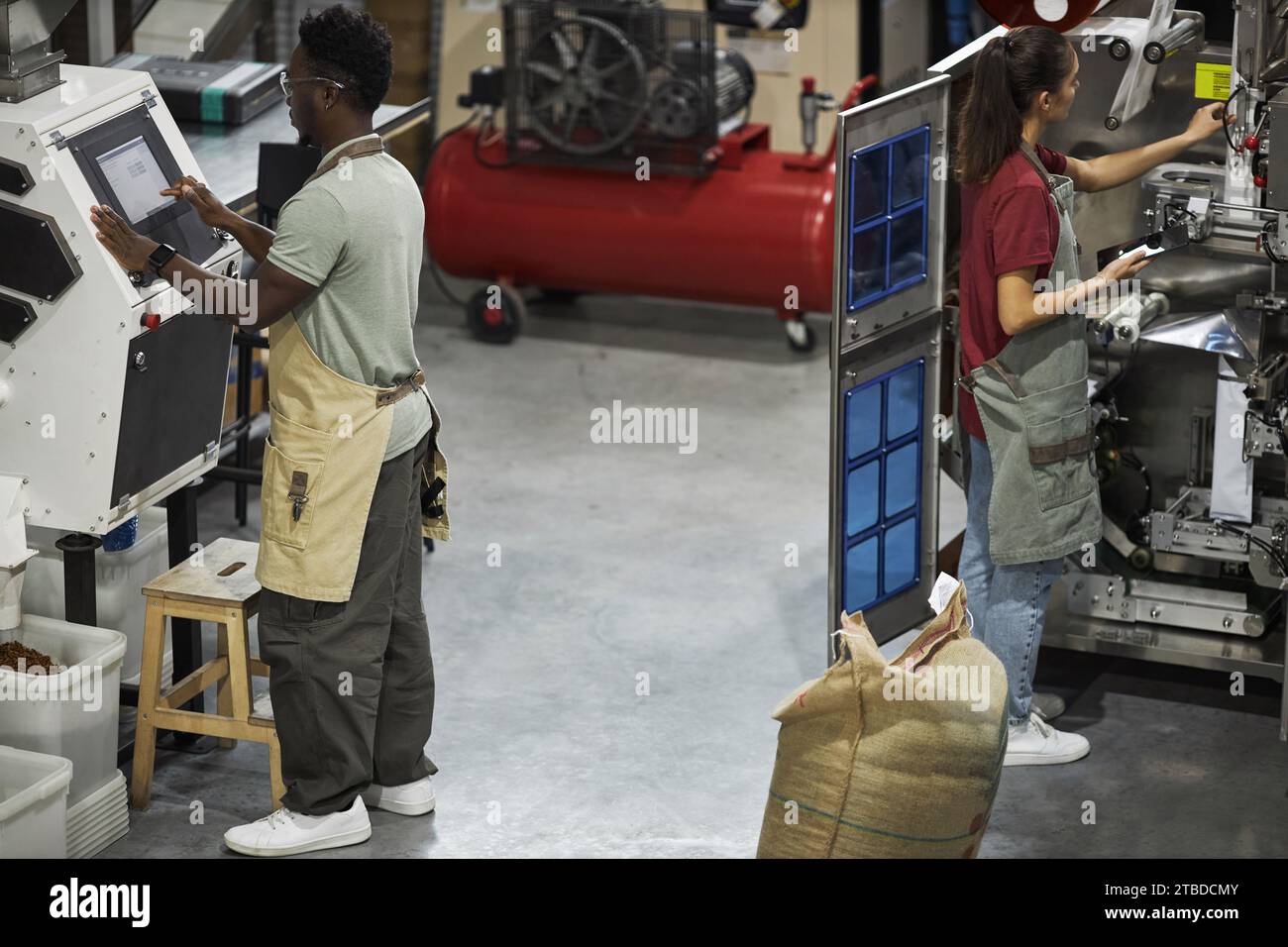 Two young people operating machines in food factory workshop, coffee ...